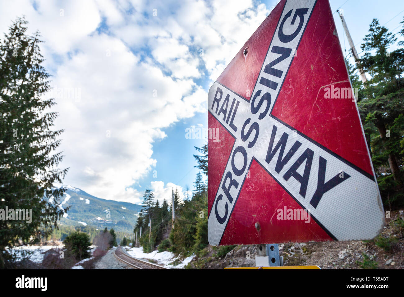 A red railway crossing sign with railroad tracks and a mountain in the ...