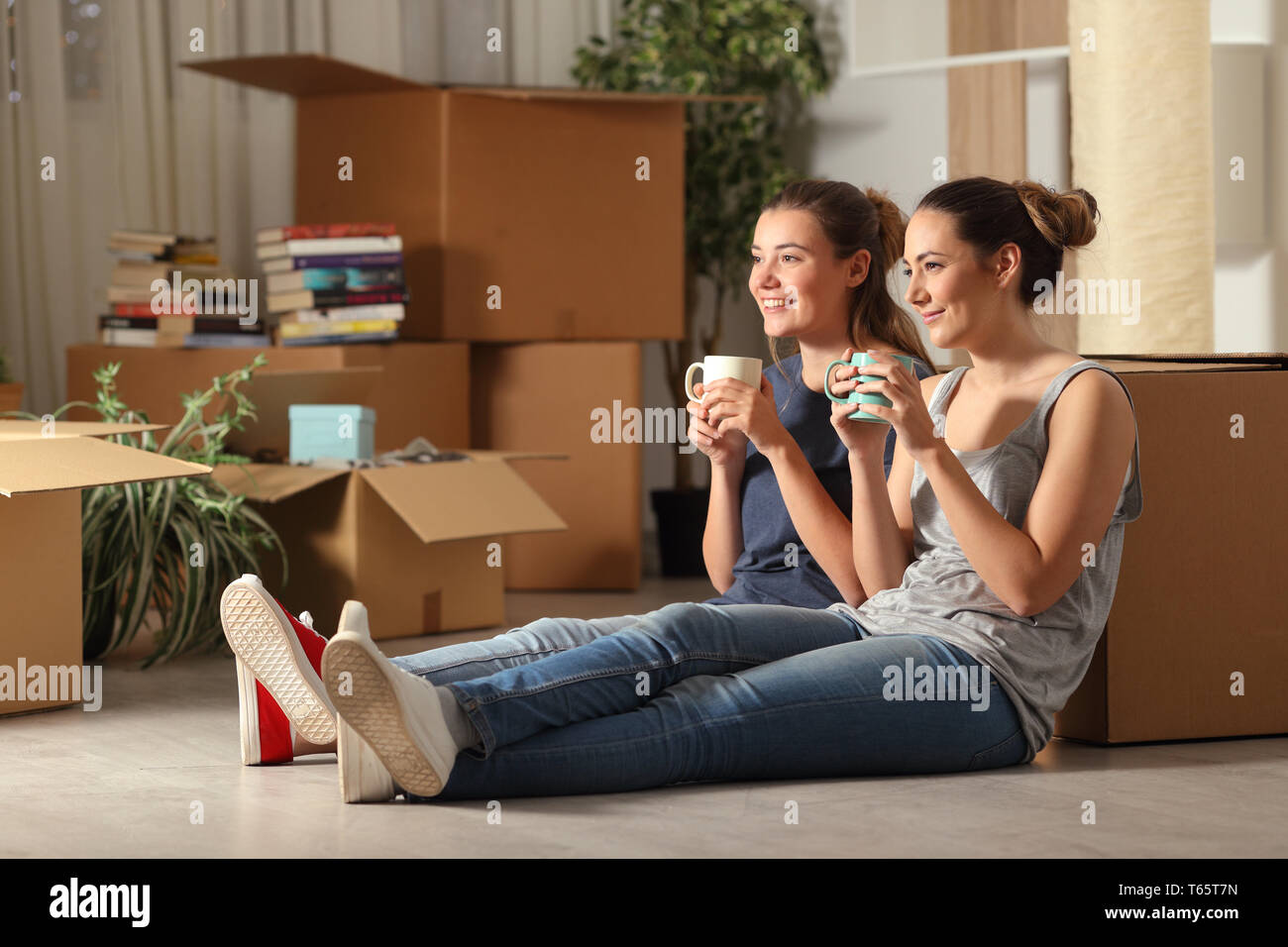 Two happy roommates moving home resting drinking coffee sitting on the ...