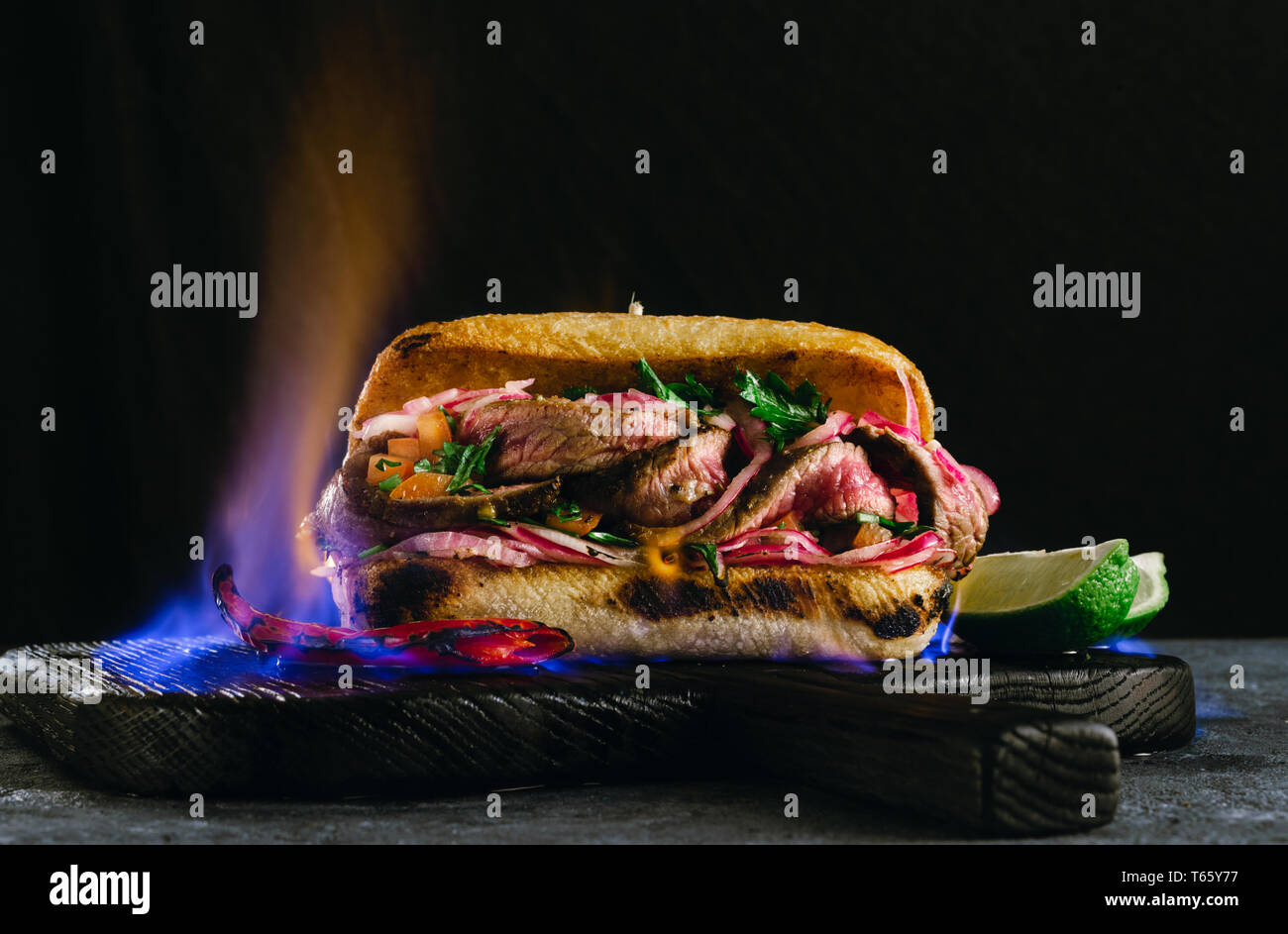 Grilled spicy steak sandwiches steak in fire flame on wooden cutting ...