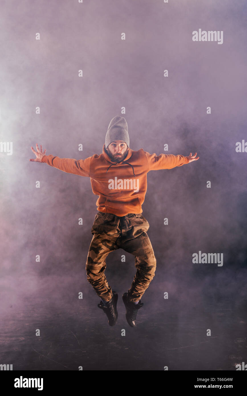 Male breakdancer jumps off high in the air while performing a cool dance move, a lot of smoke in ...