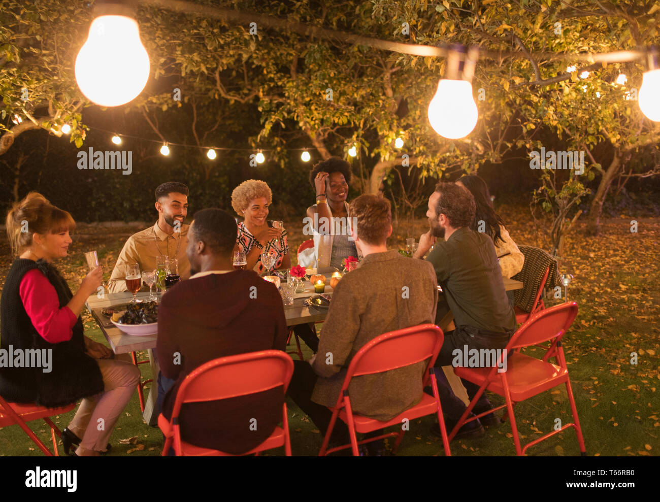 Friends enjoying dinner garden party under trees with fairy lights ...