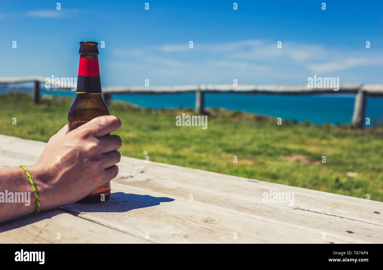 Vacation concept. Male hand holding bottle of beer on the sea beach on ...