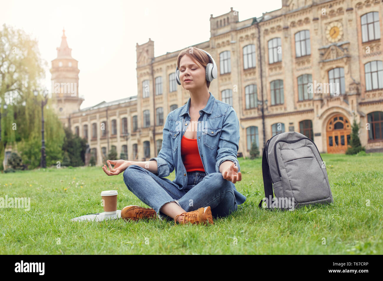 Young female student wearing headphones at university campus sitting on ...