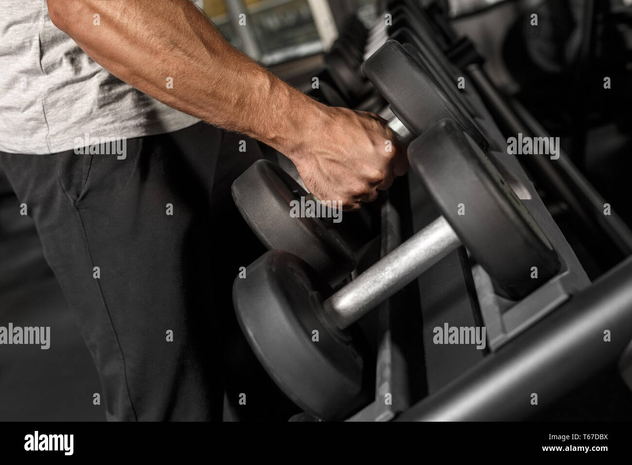 Man bodybuilder at gym standing taking dumbbell from stand for exercise ...