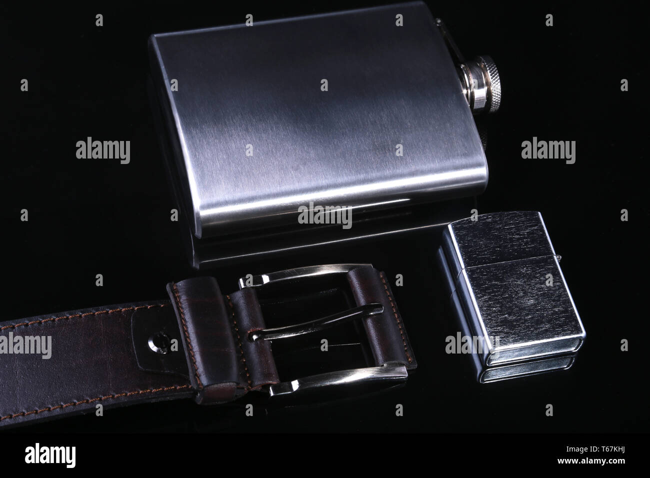 Stainless hip flask, lighter and luxury belt isolated on mirror black ...