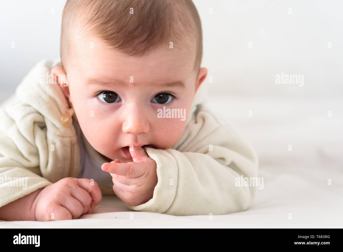 Portrait of an adorable smiling baby biting her own fingers putting her ...