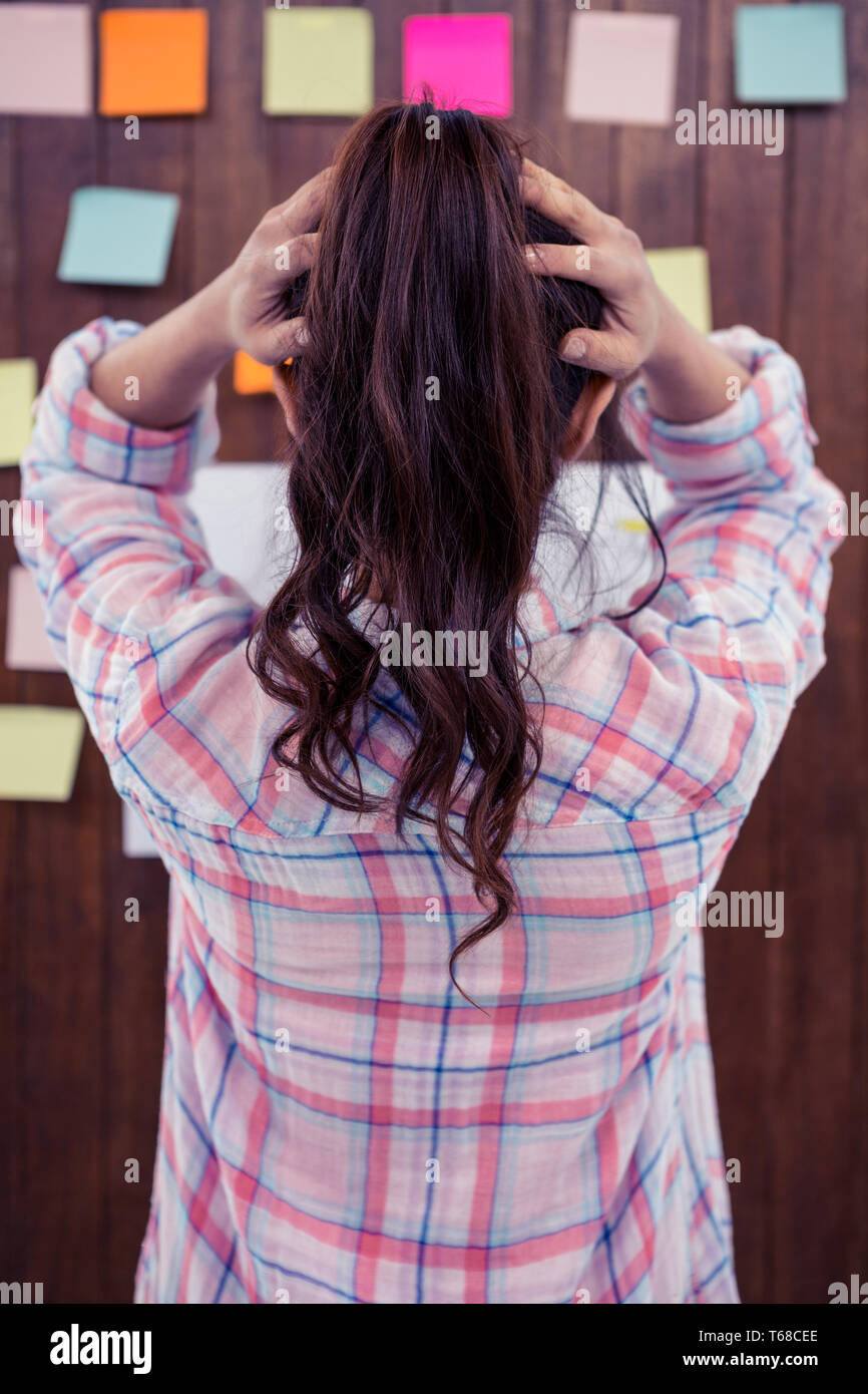 Brunette with hands on hair in front of sticky notes on wooden wall ...