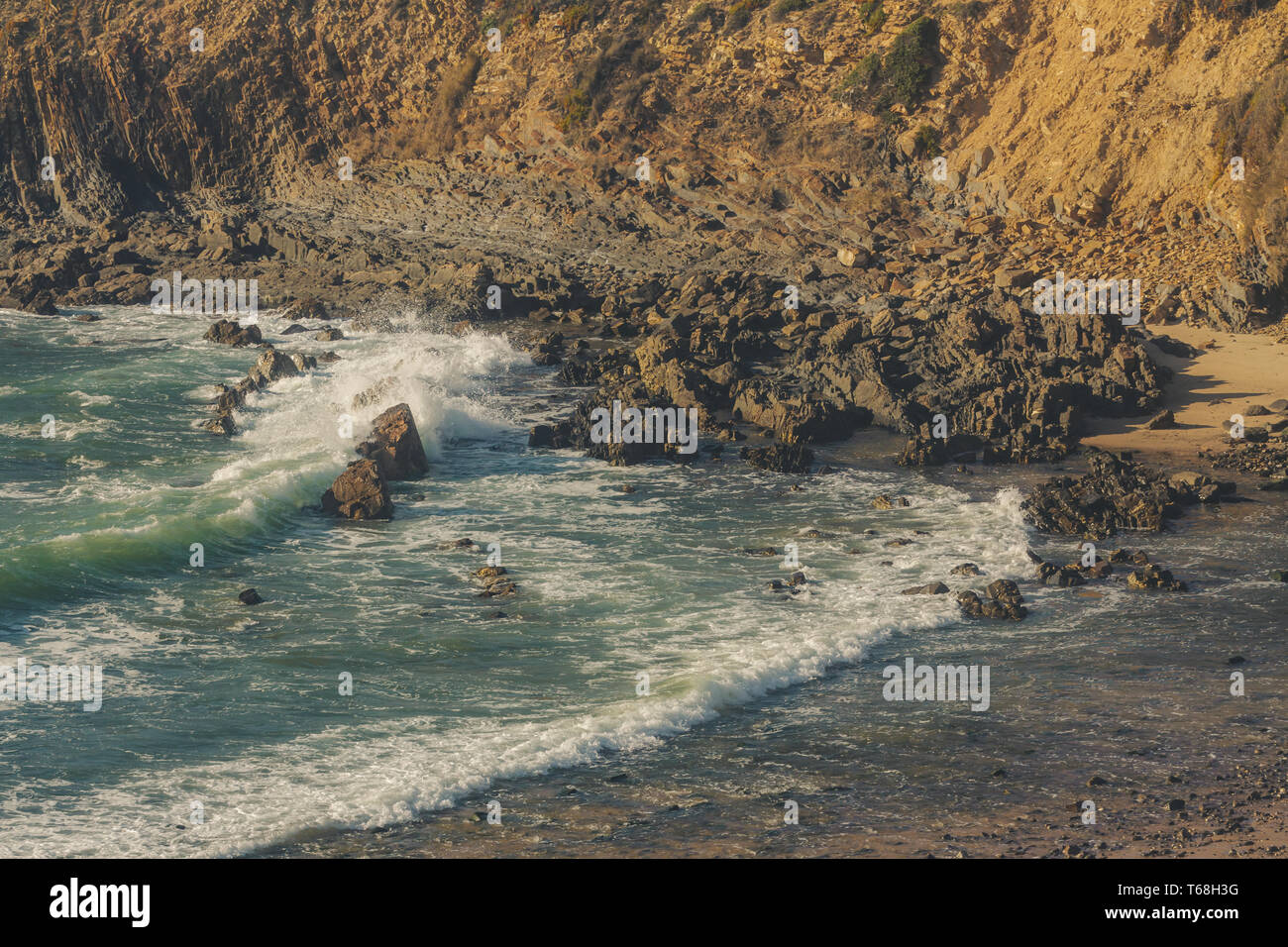 Two waves crashing on the rocks near of the cliff on the beach ...