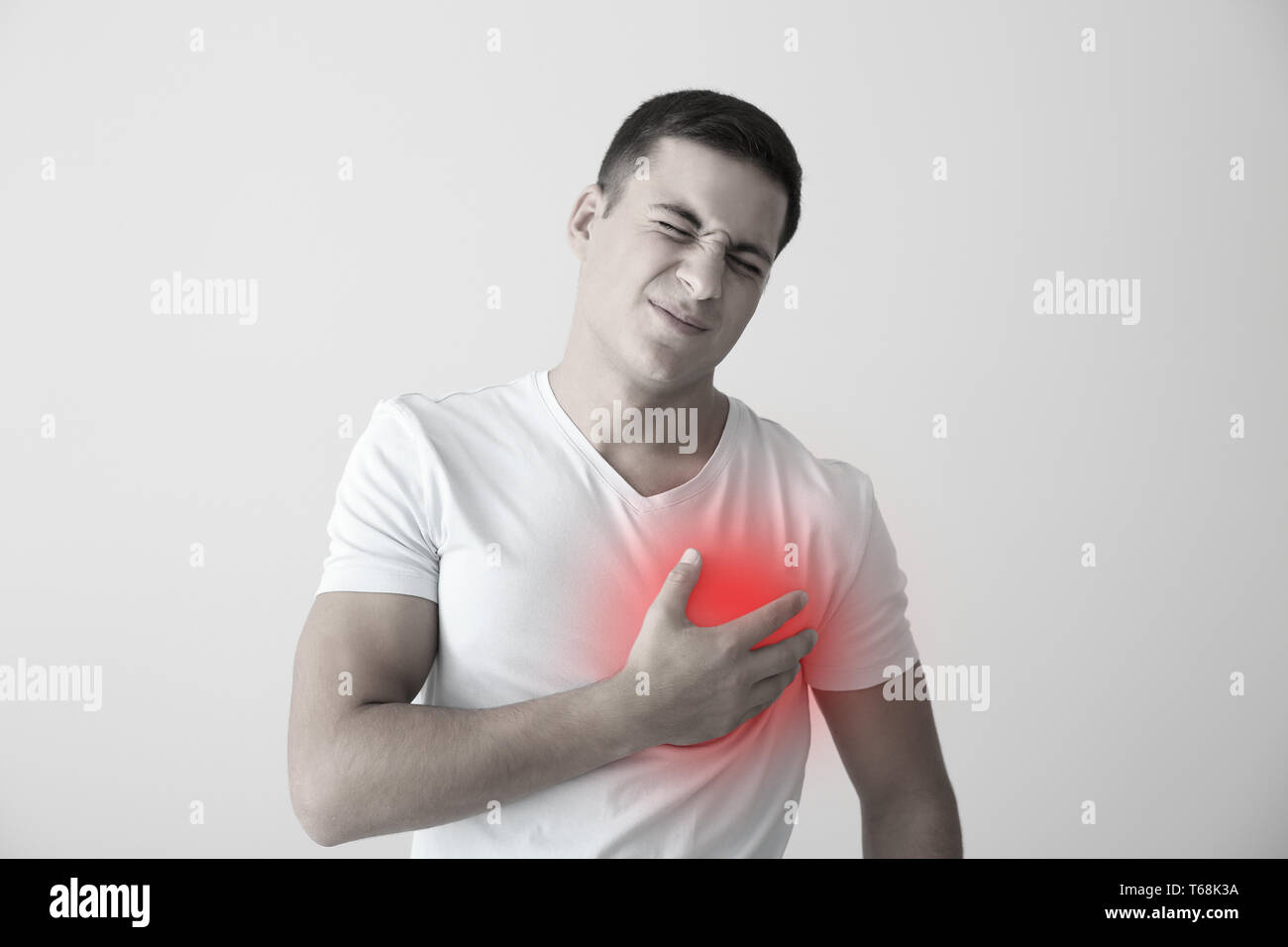 Young man suffering from heart attack on light background Stock Photo ...