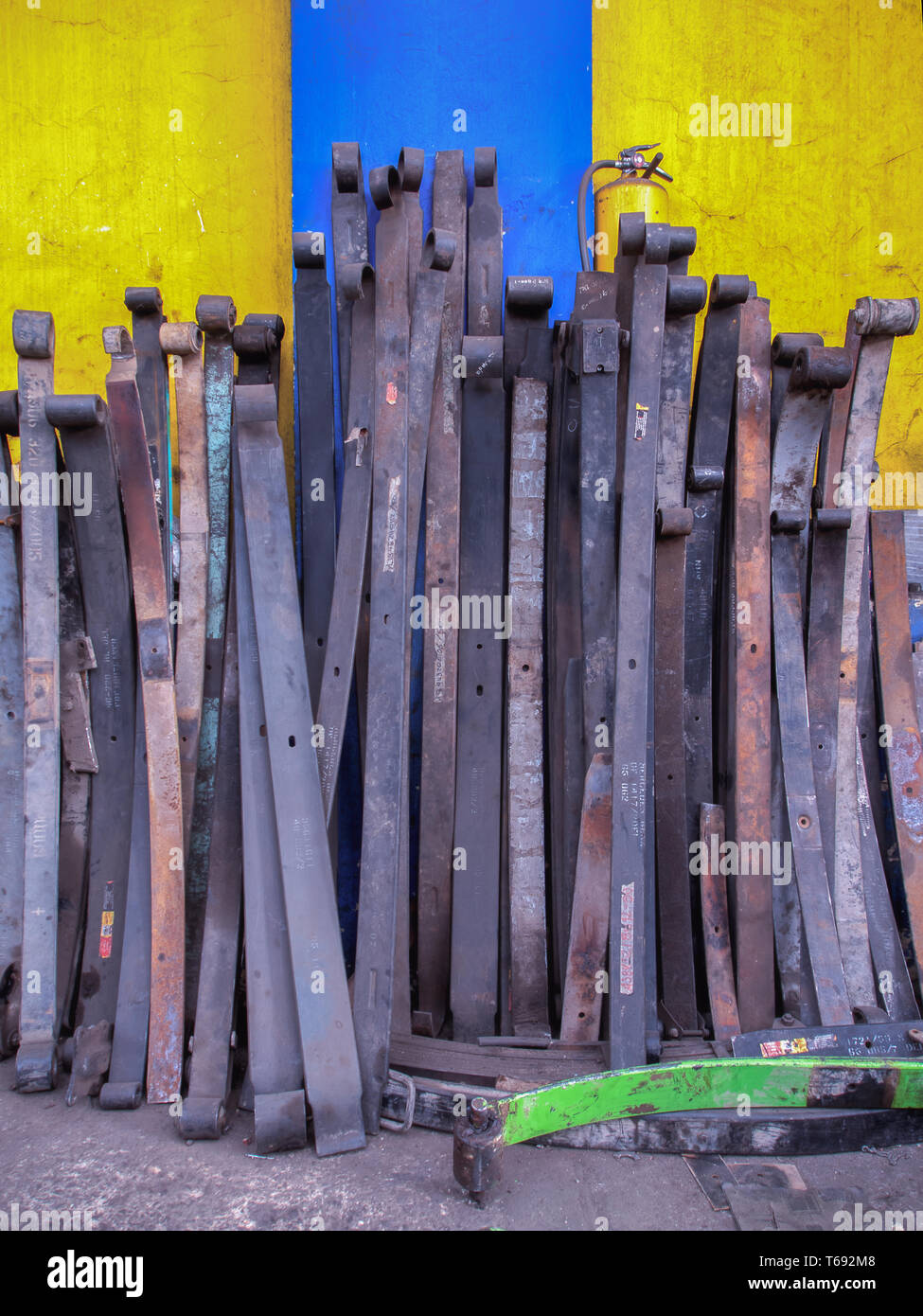 A group of leaf springs against a colorful wall, in a messy auto repair ...