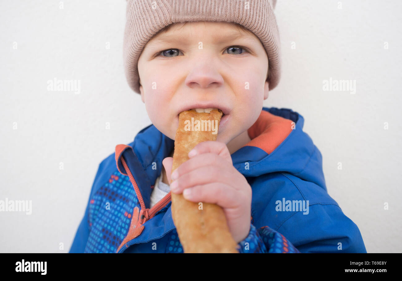 Little toddler biting traditional spanish churro outdoors. He is ...