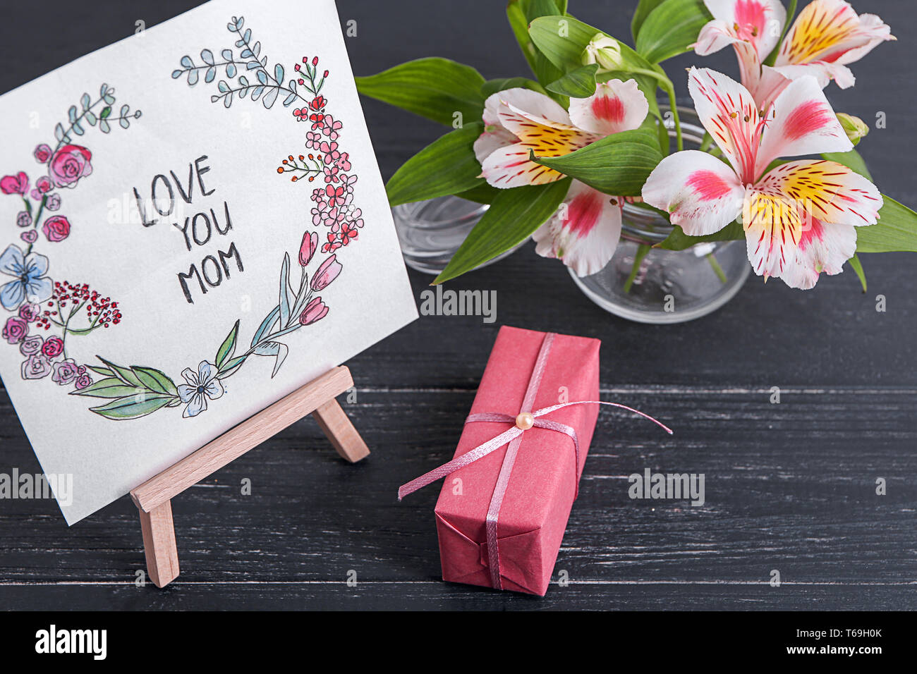 Card with phrase "Love you mom", flowers and gift box on table ...