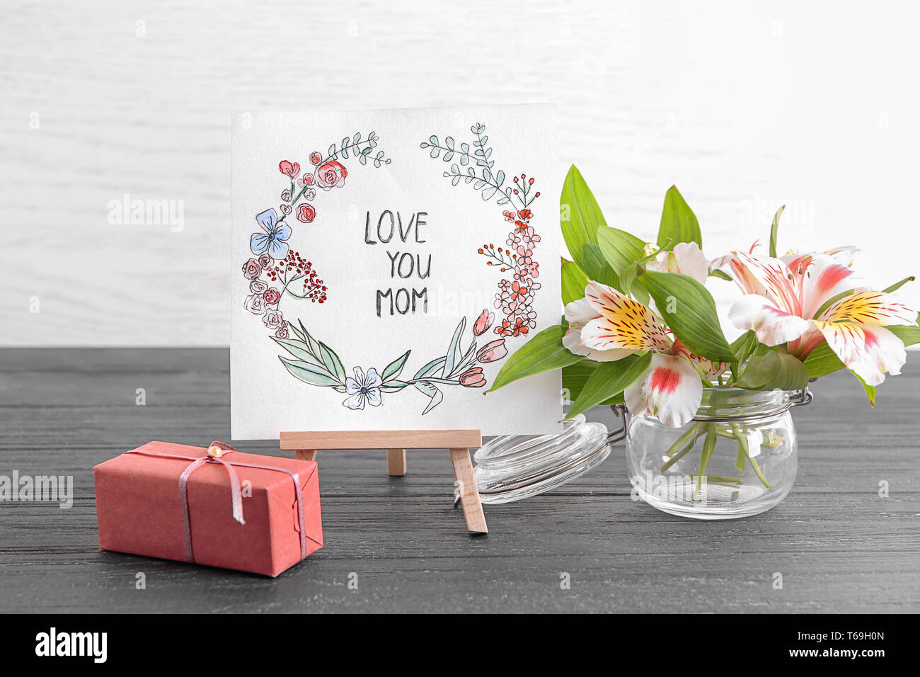 Card with phrase "Love you mom", flowers and gift box on table ...