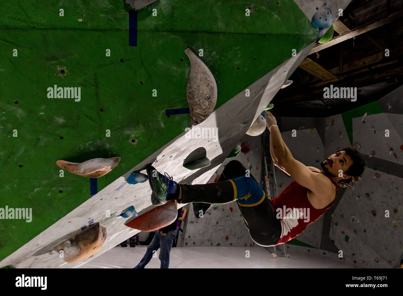Rock climber man hanging on a bouldering climbing wall, inside on ...