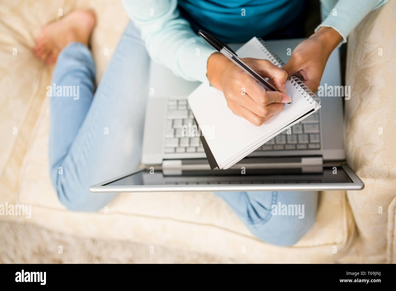 Mid section of woman writing on notepad with laptop on her legs Stock ...