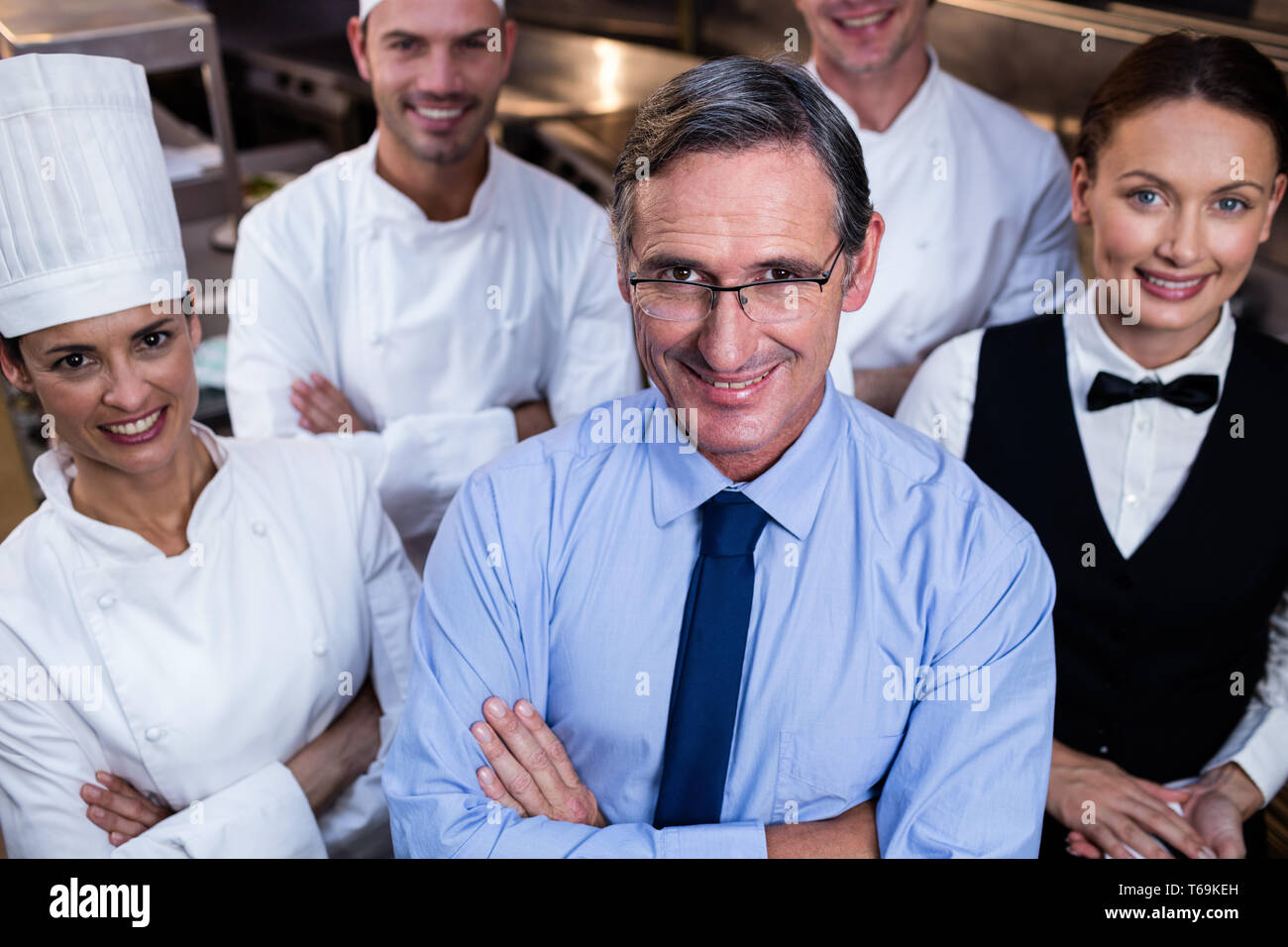 Happy restaurant team standing together with arms crossed in commercial ...