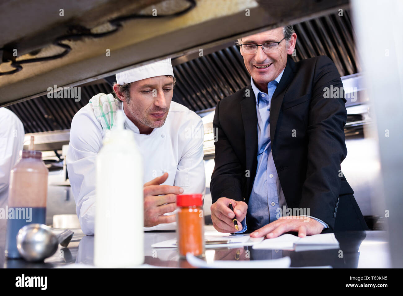 Male restaurant manager writing on clipboard while interacting to head ...