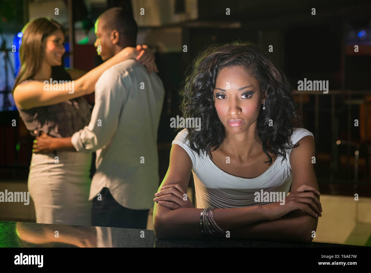 Unhappy woman sitting at bar counter and couple dancing behind her ...