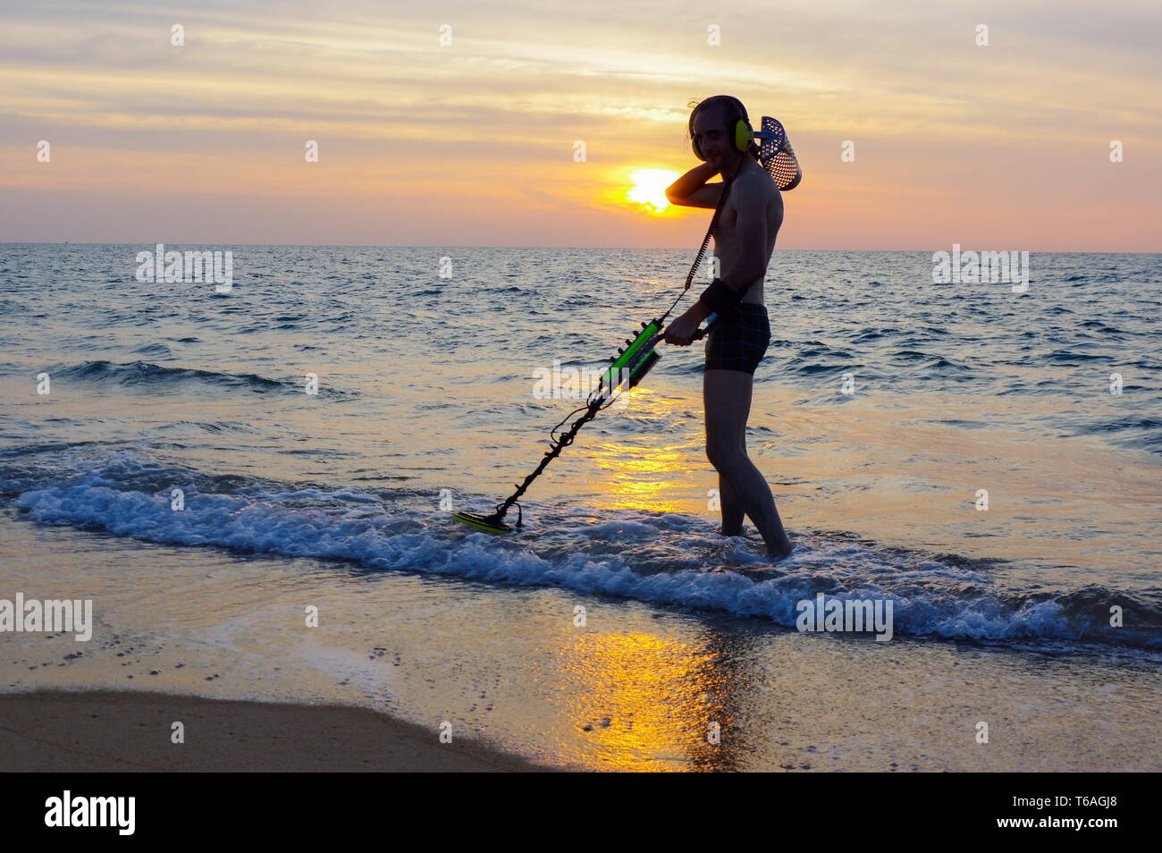 Treasure hunter with Metal detector on sunset the beach Stock Photo - Alamy