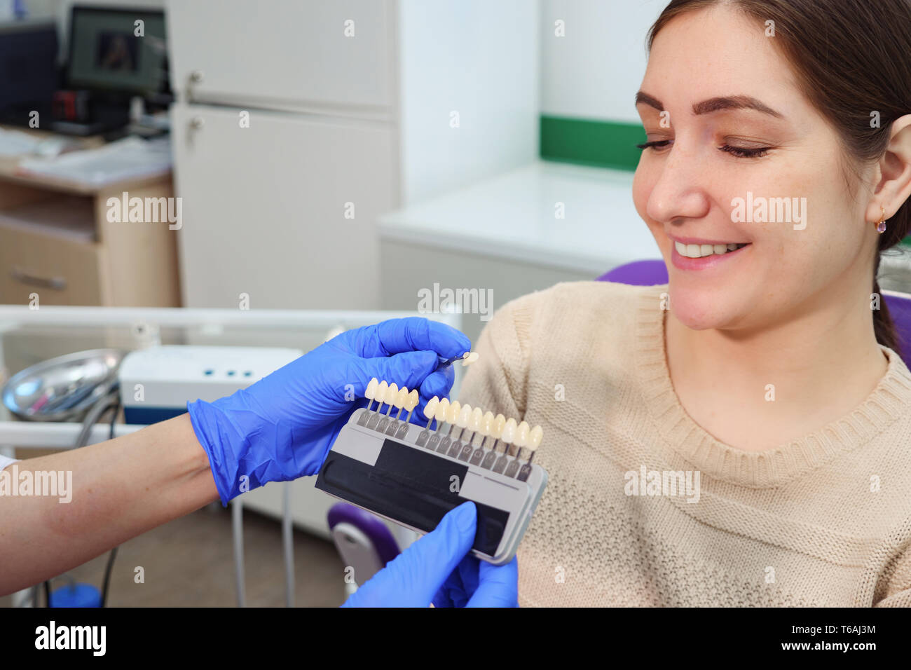 Dentist with tooth color samples is choosing shade for women patient ...