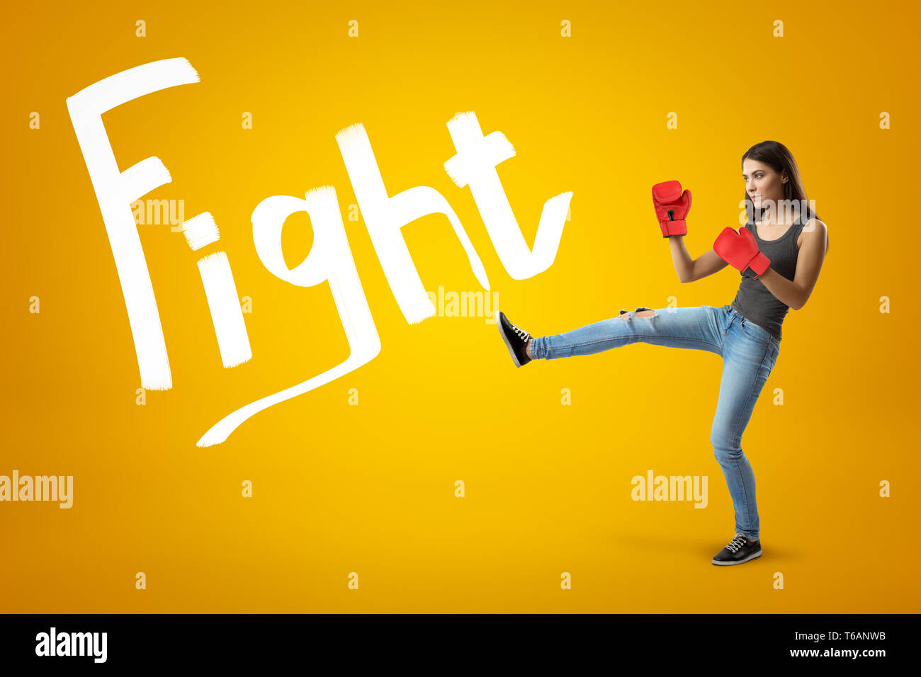 Side view of young pretty girl in jeans, sleeveless top and red boxing ...