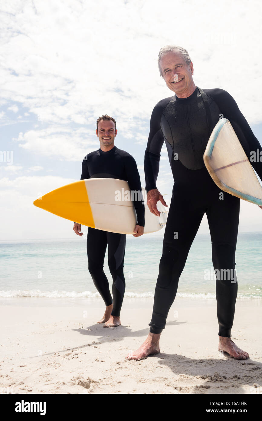 Portrait of happy father and son standing with surfboard on the beach ...