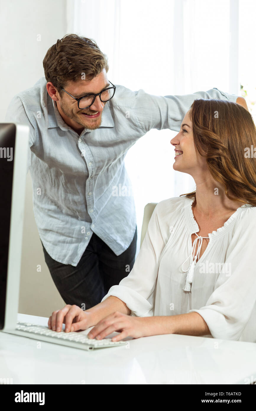 Male and female collegues smiling while using computer at office desk ...