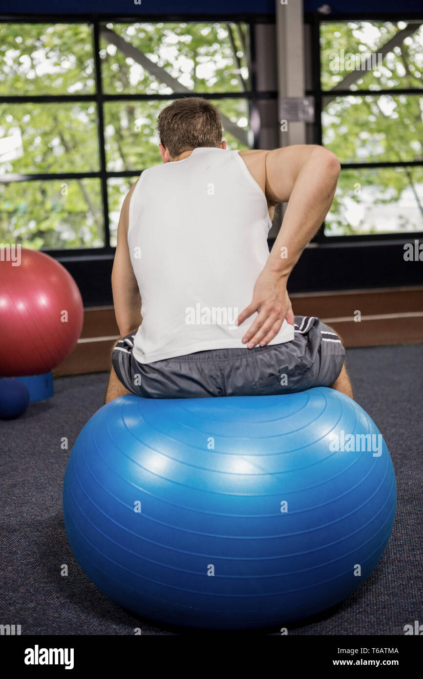Rear view of man touching his back sitting on fitness ball Stock Photo ...