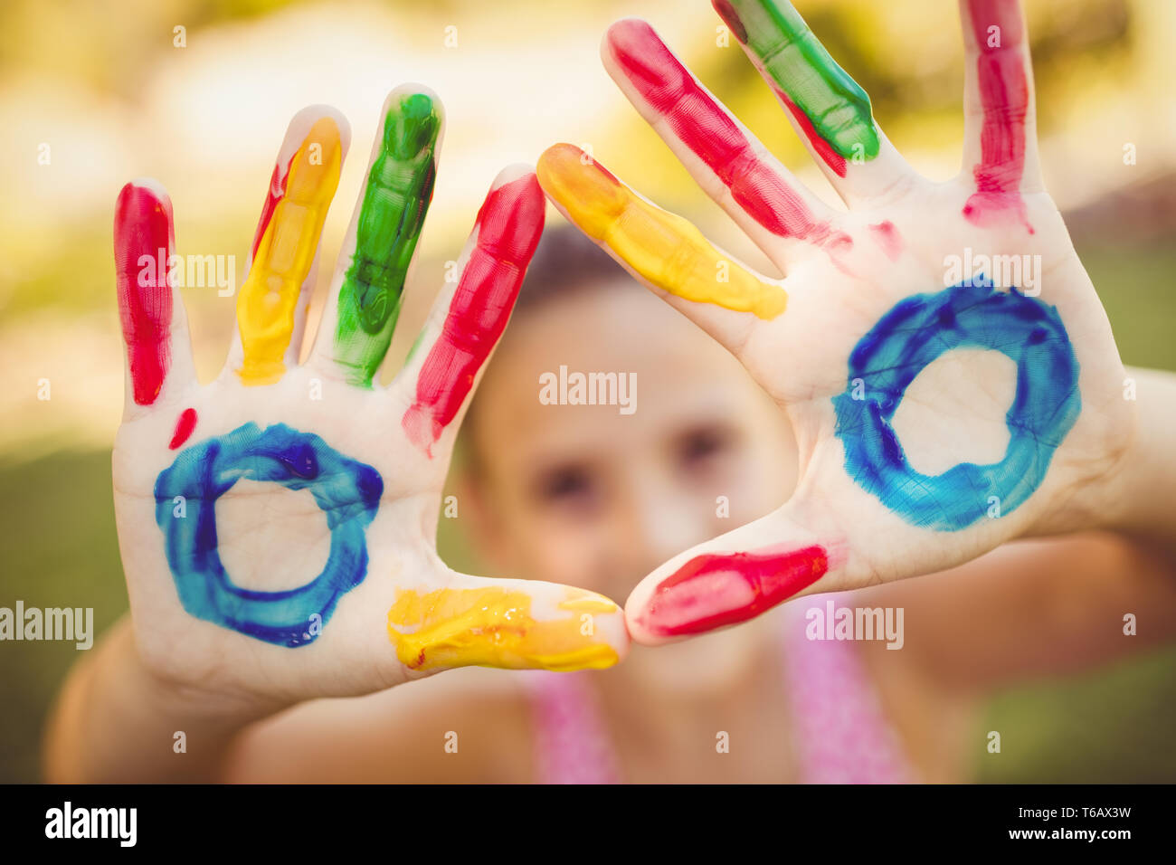 Little girl making a triangle with her painted hands to the camera ...