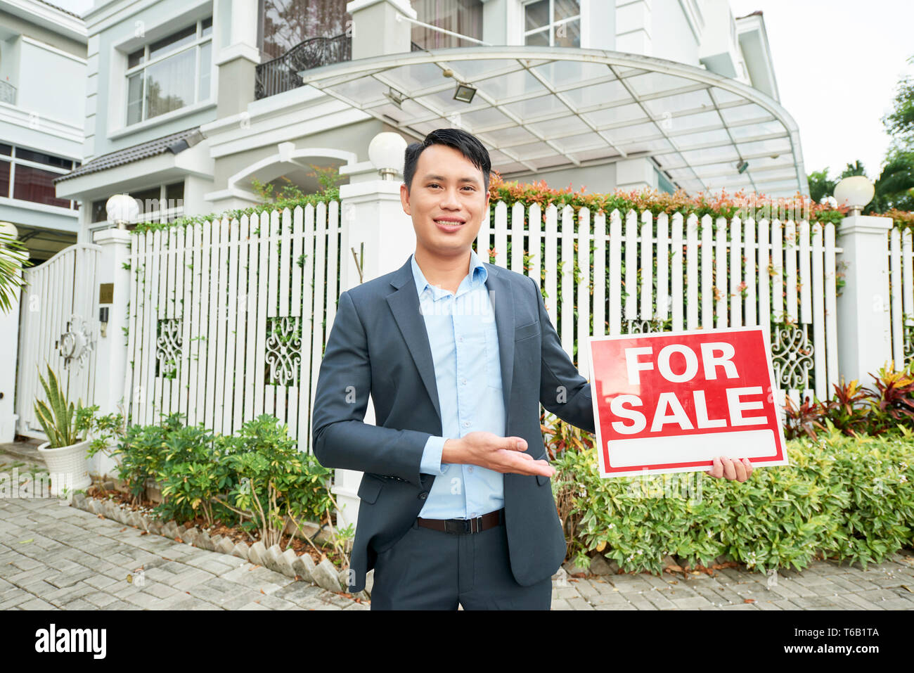 Realtor standing with sale sign Stock Photo - Alamy