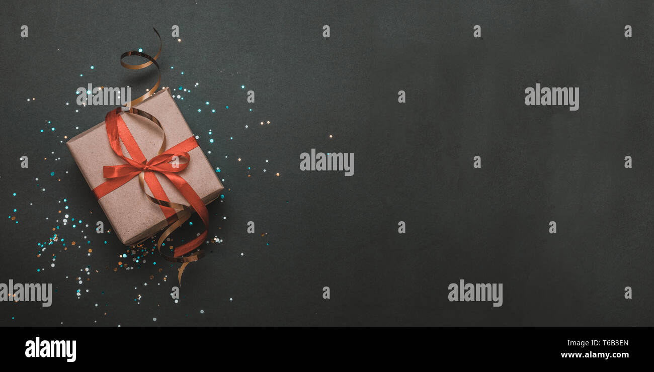 Birthday gift box with red ribbon and gold confetti on a dark contrast ...