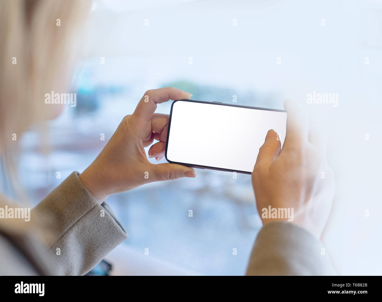 Woman with modern mobile phone in hands touching on a blank screen ...