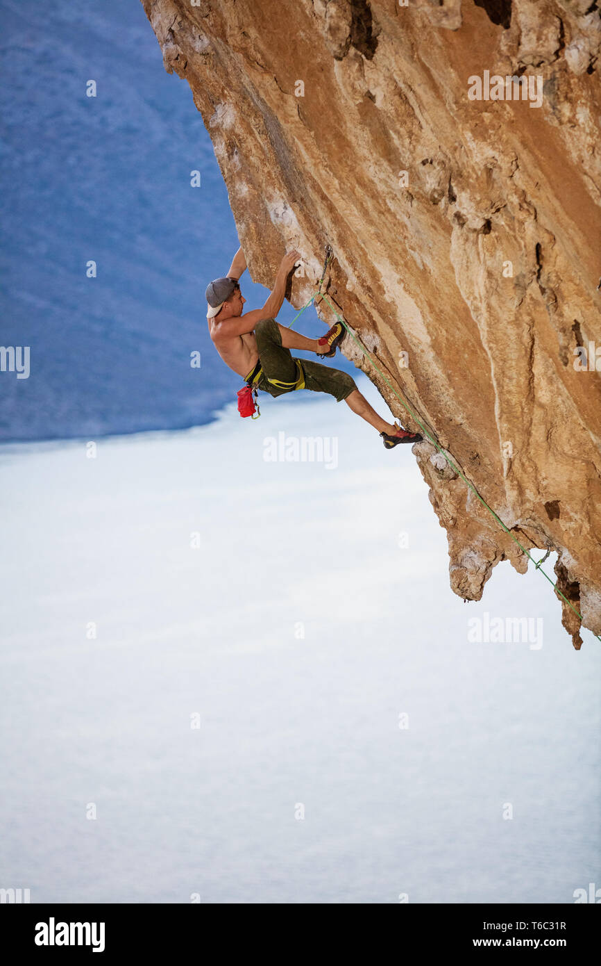 Caucasian young man climbing challenging route on overhanging cliff ...