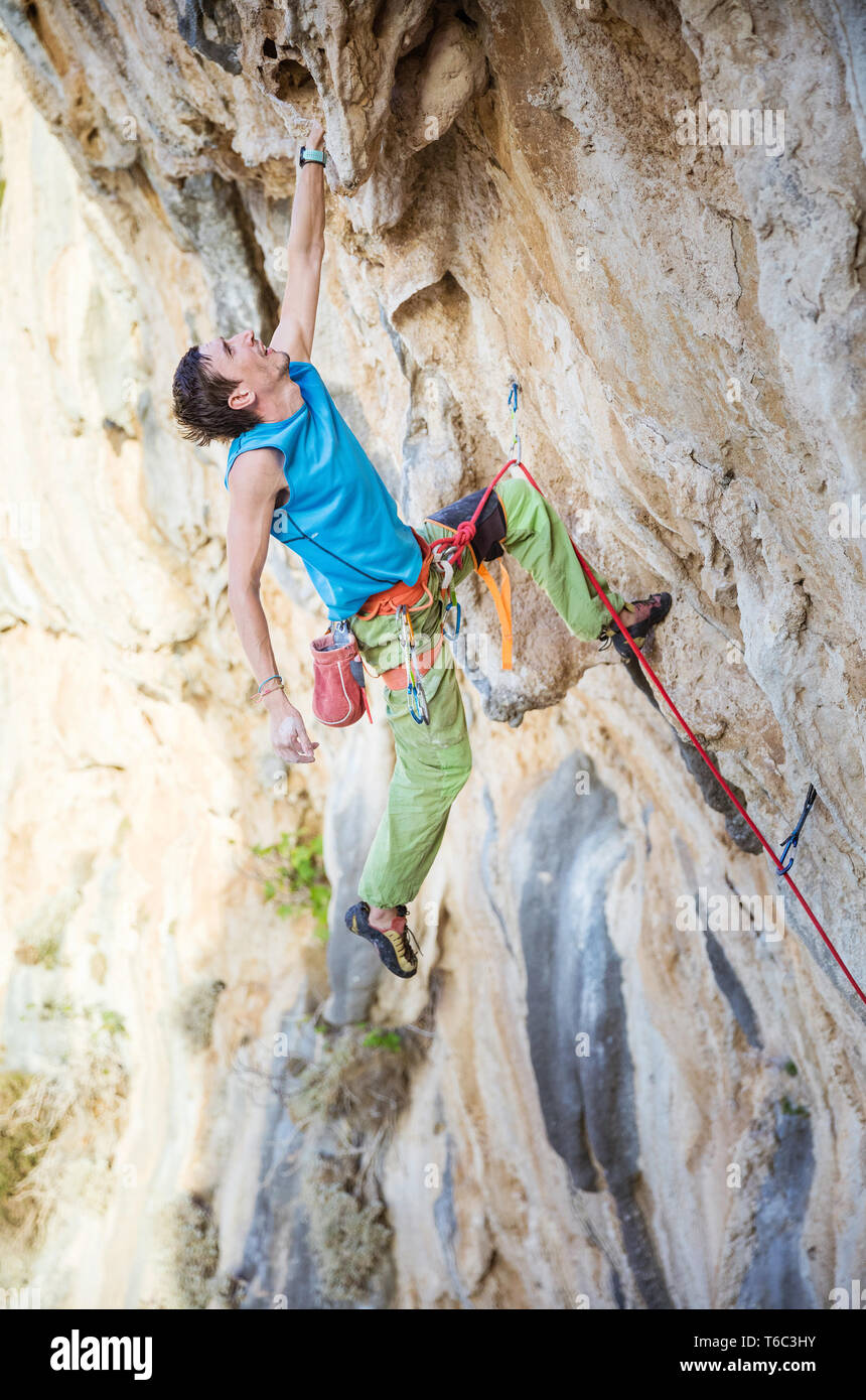 Caucasian young man climbing challenging route on overhanging cliff ...