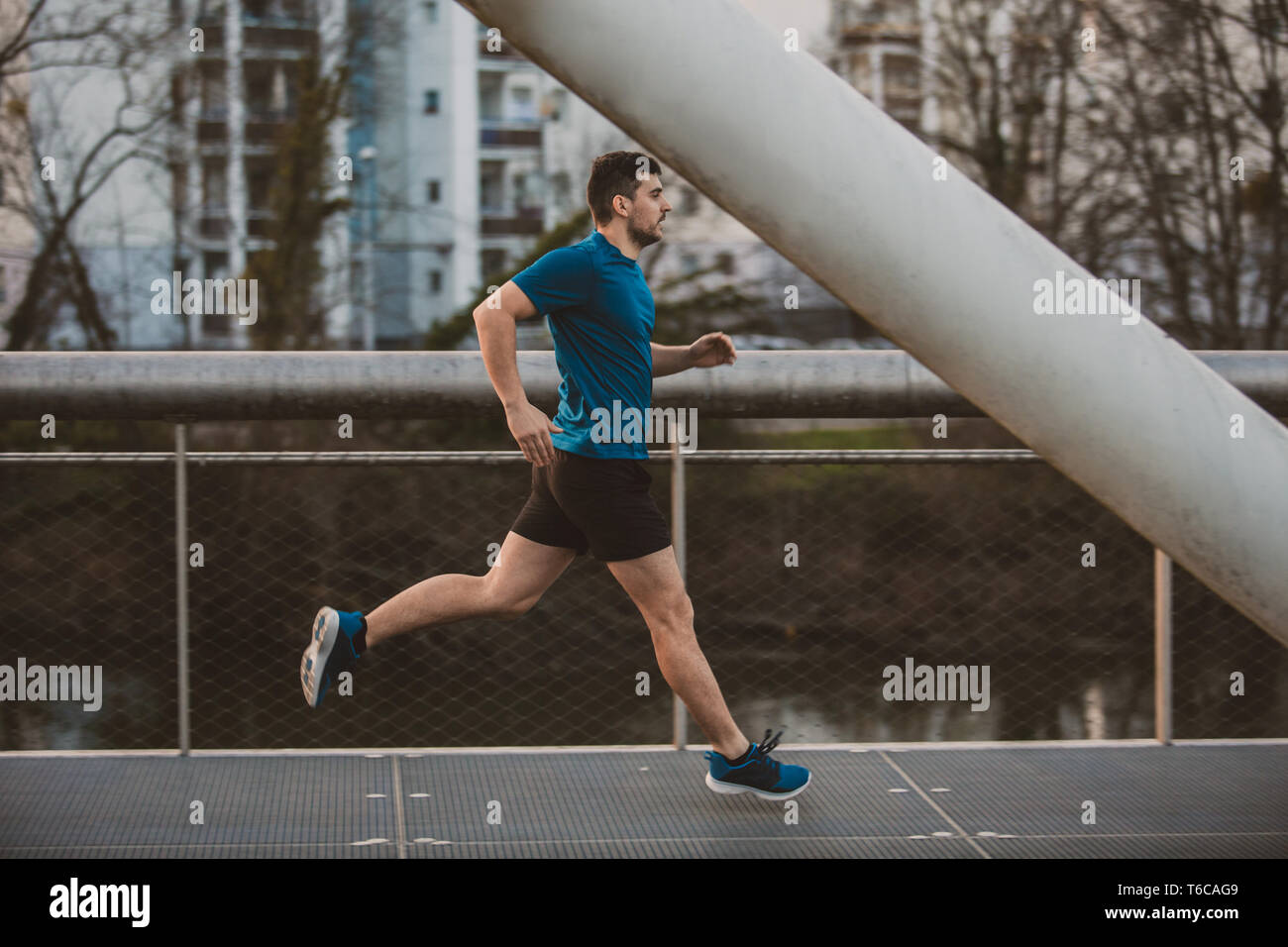 Young athletic man practicing sport outdoors, running fast along bridge ...