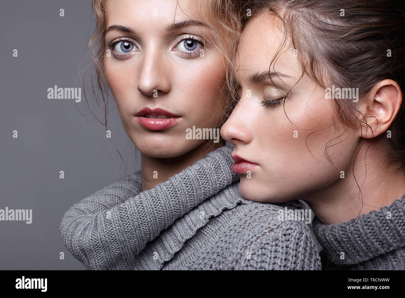 Two young women in gray sweaters on grey background. Beautiful girls ...