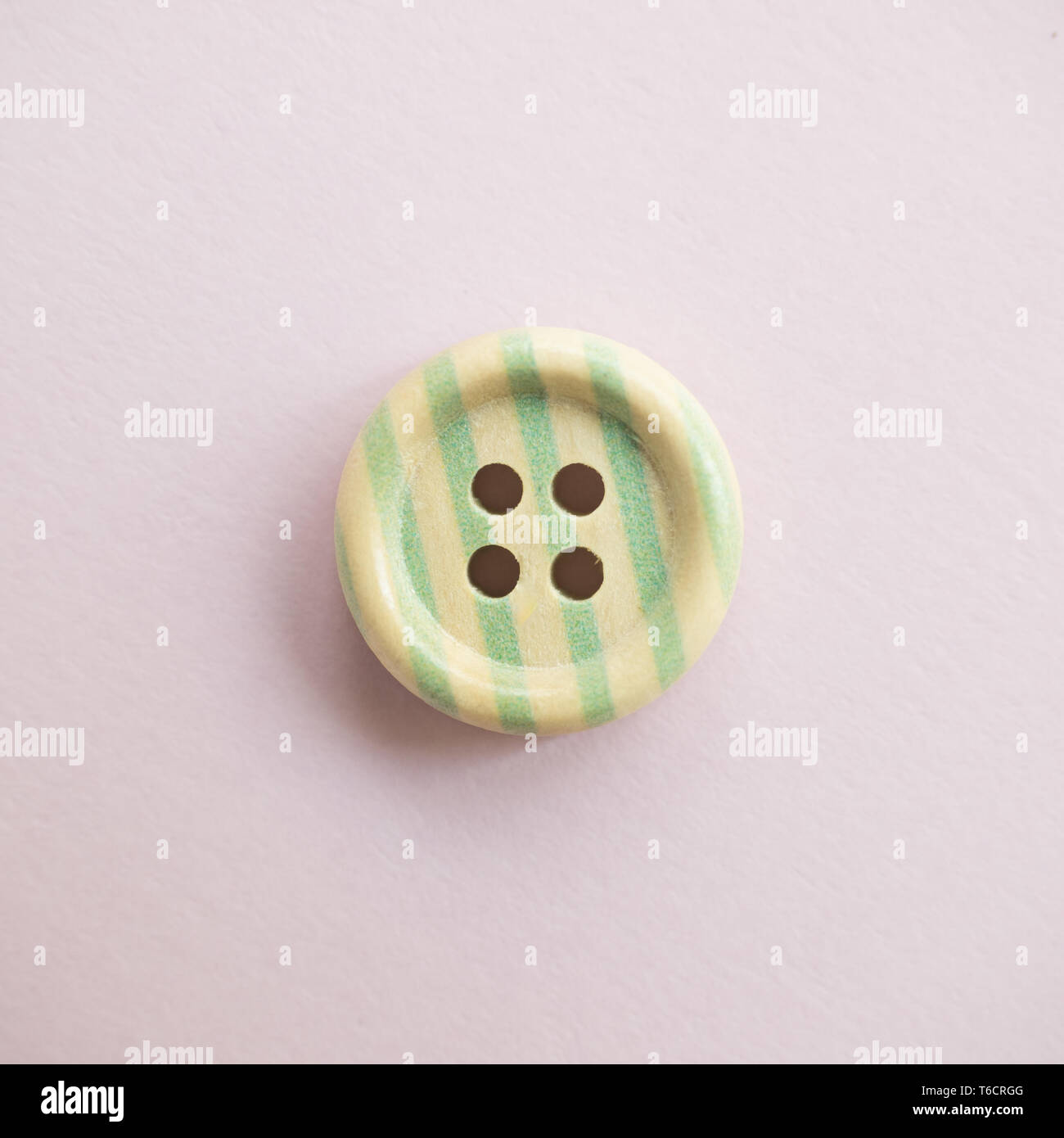 Isolated wooden button with colored colorful stripes on a light pink ...