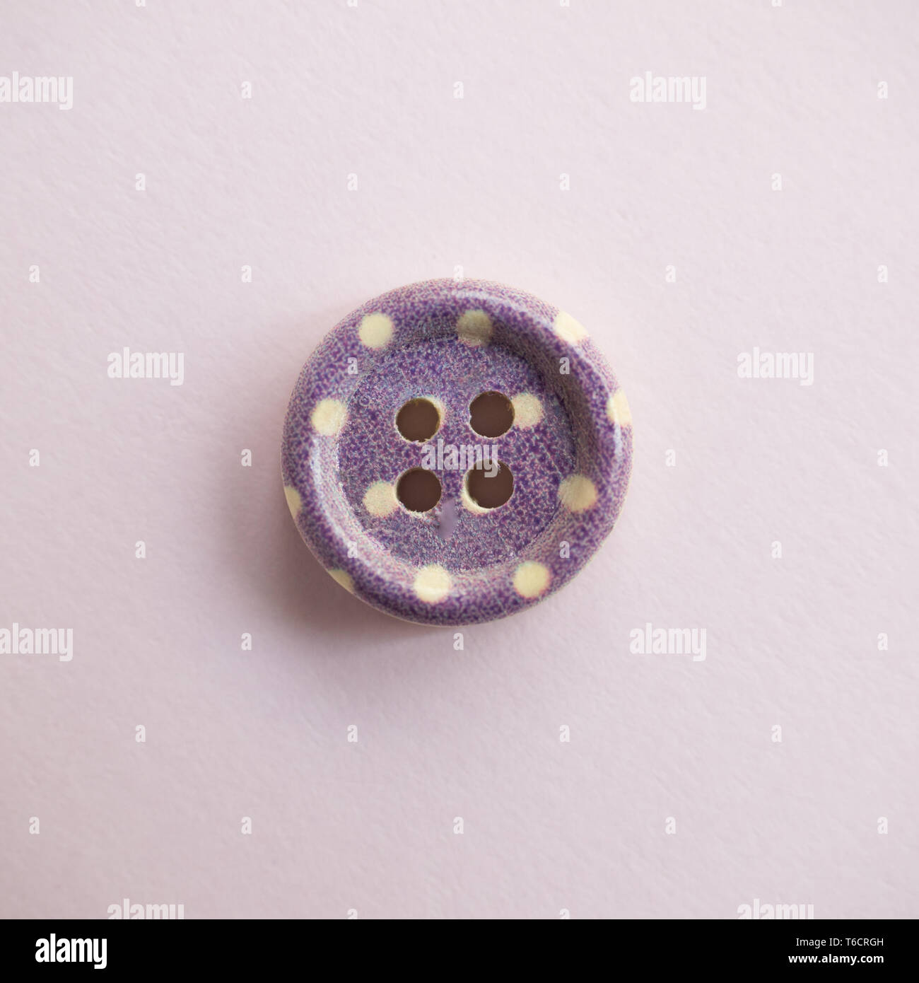 Isolated wooden button with colored colorful dots on a light pink ...