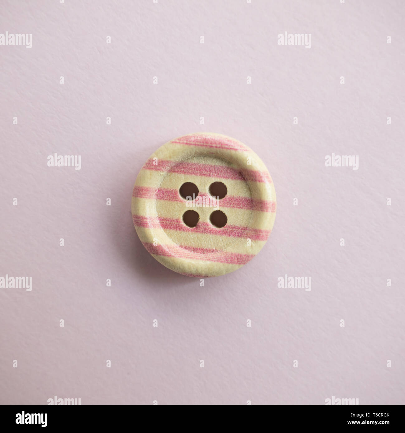 Isolated wooden button with colored colorful stripes on a light pink ...