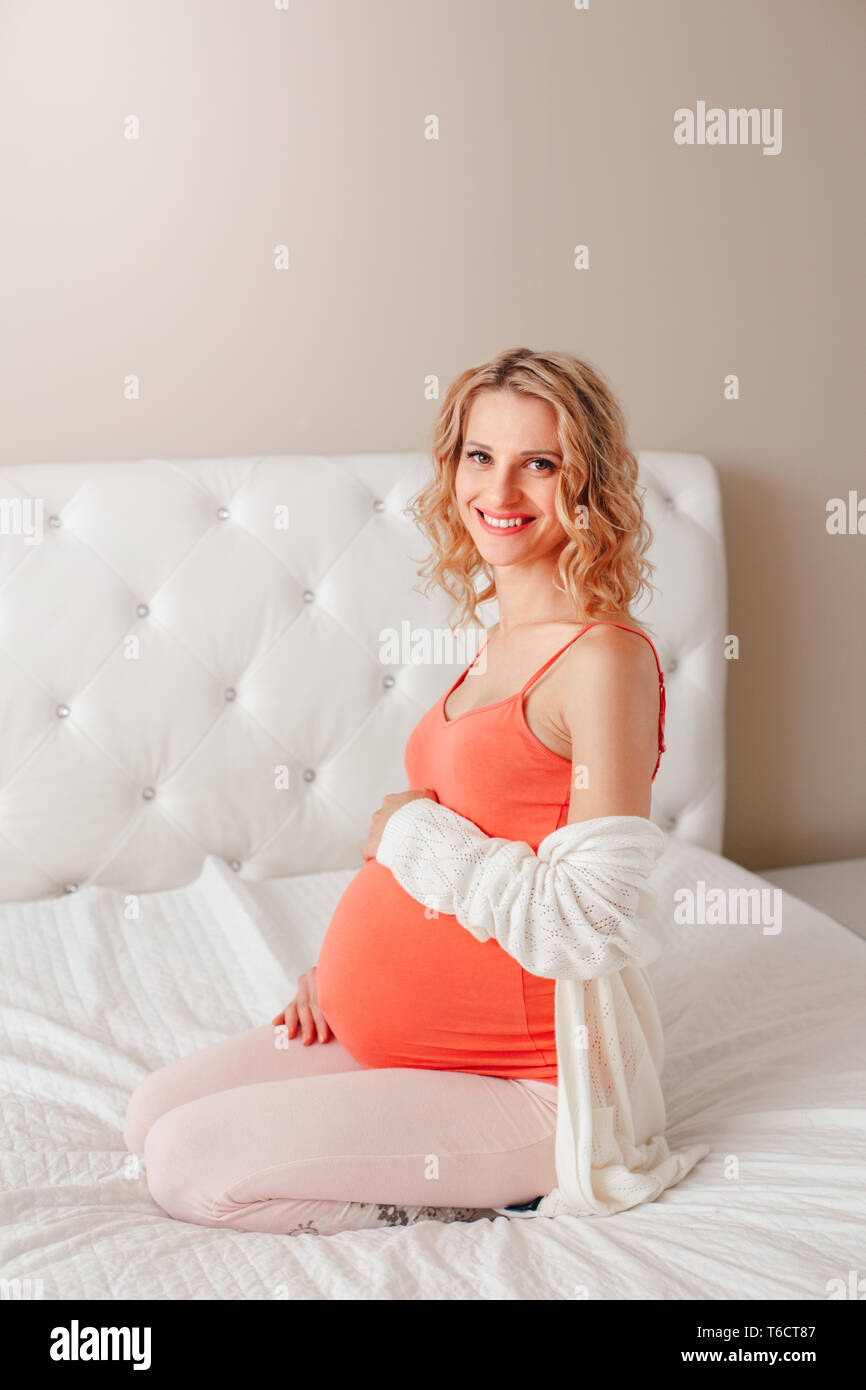 Portrait of smiling white Caucasian blonde pregnant woman touching her ...
