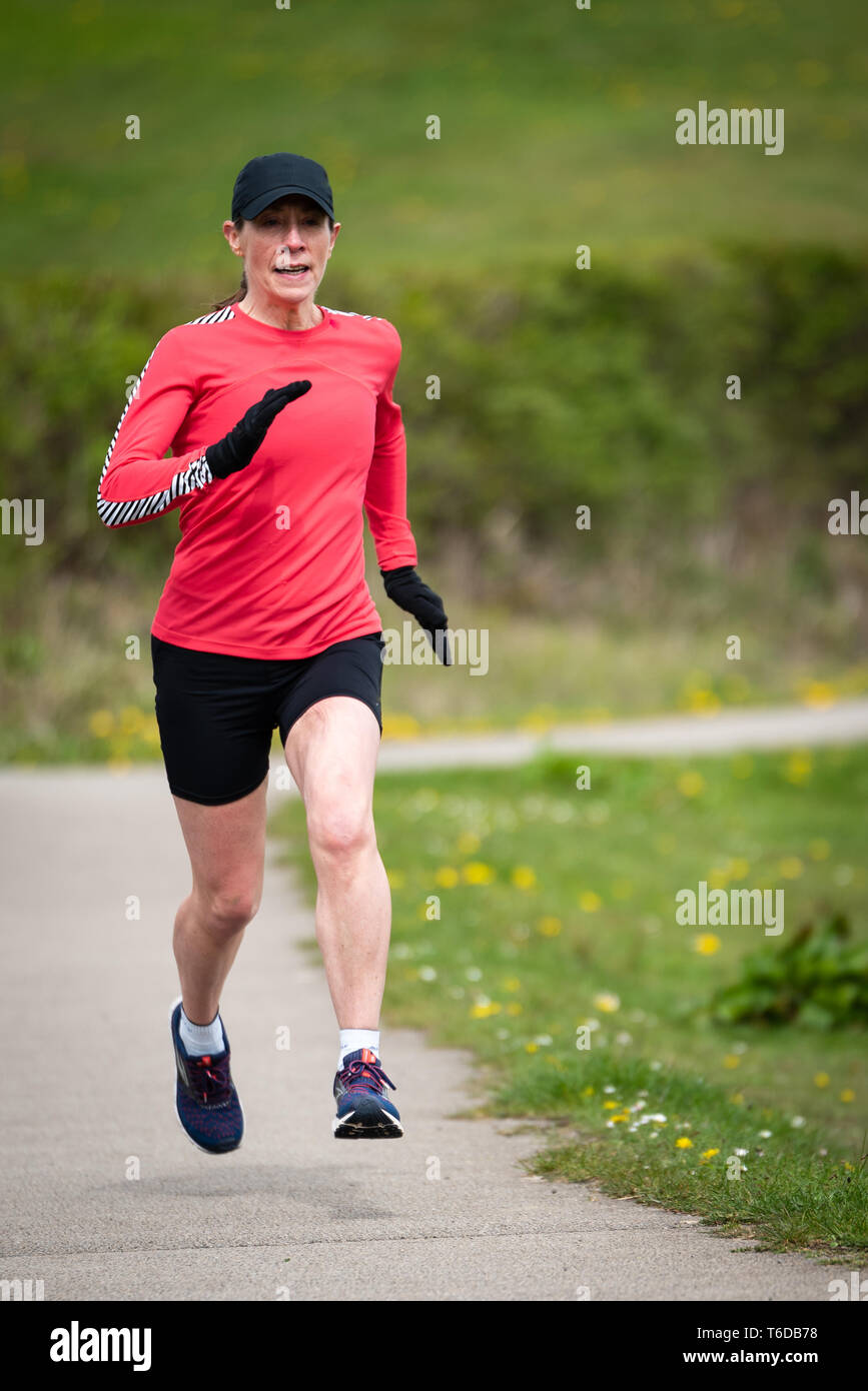 Fit senior woman in 50s exercising and keeping fit by running in a park ...
