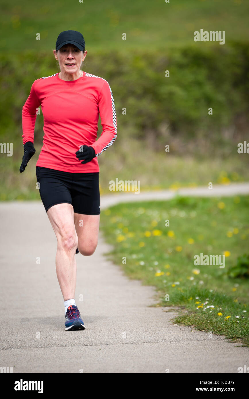 Fit senior woman in 50s exercising and keeping fit by running in a park ...