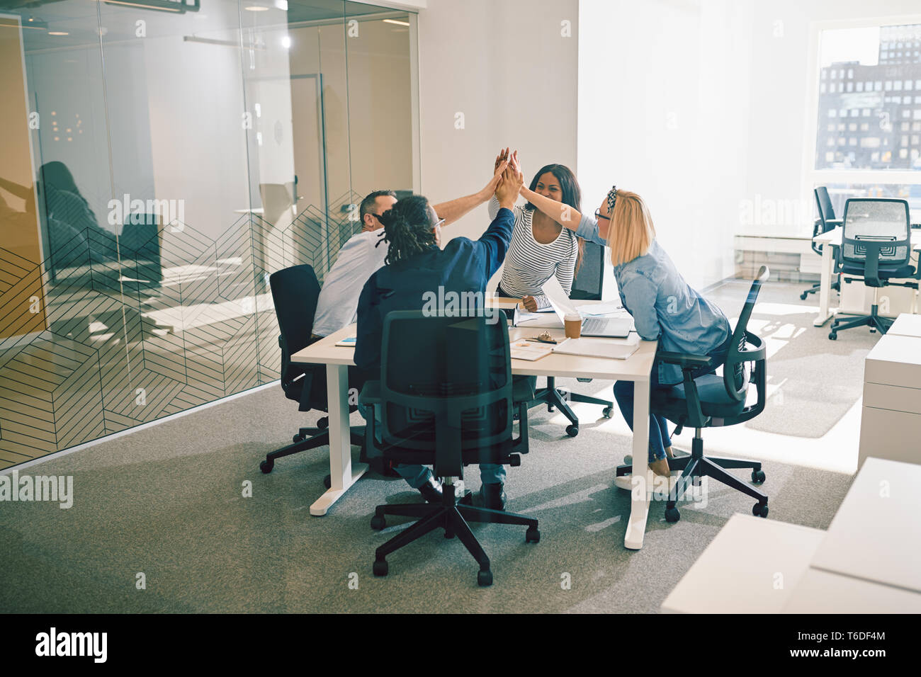 Diverse group of work colleagues smiling and high fiving together during a meeting around a ...