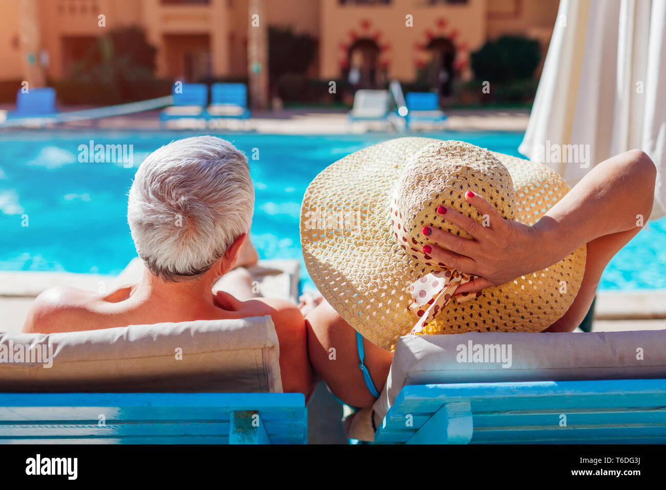 Senior family couple relaxing by swimming pool lying on chaise-longues ...