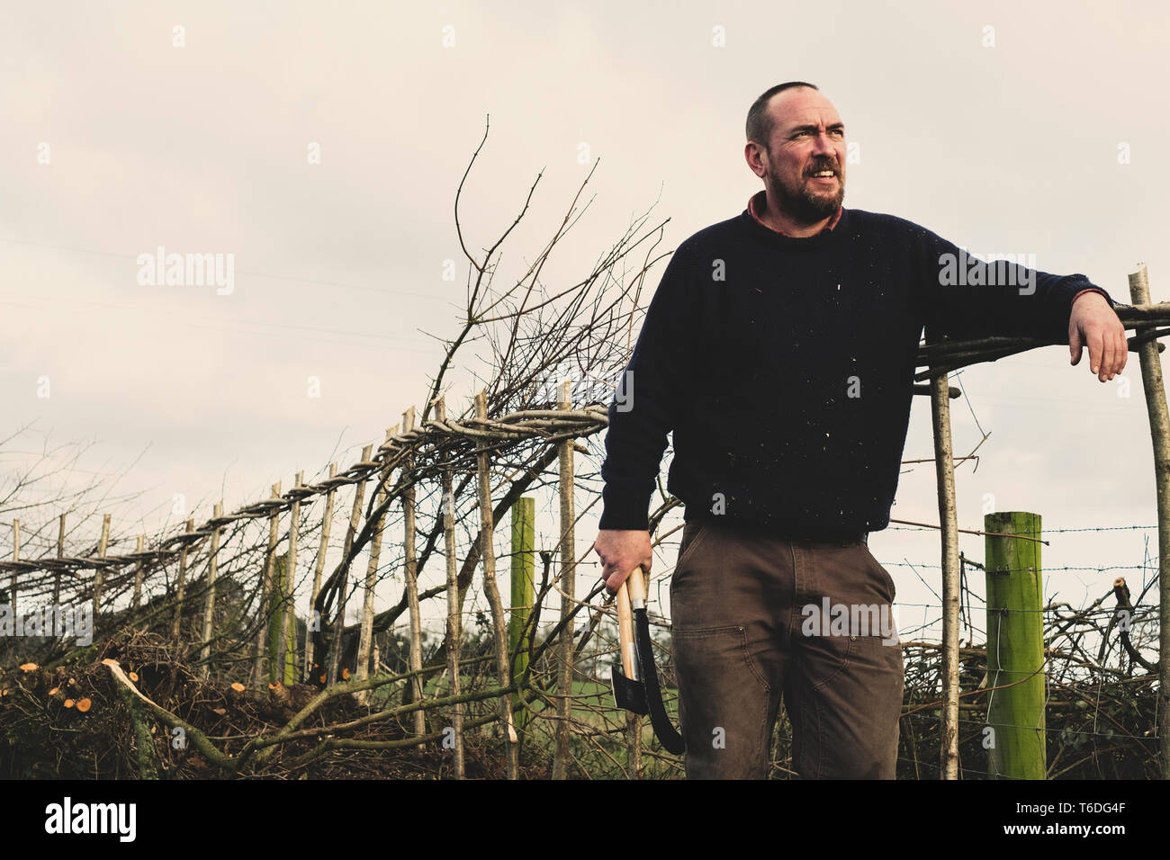 Smiling bearded man holding axe and bill hook standing next to a newly ...