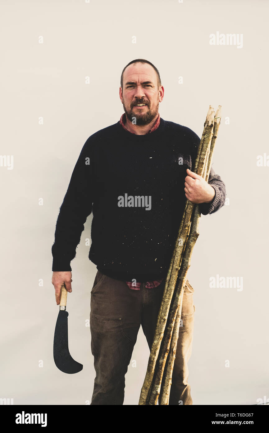 Bearded man holding bill hook and bunch of wooden stakes for ...