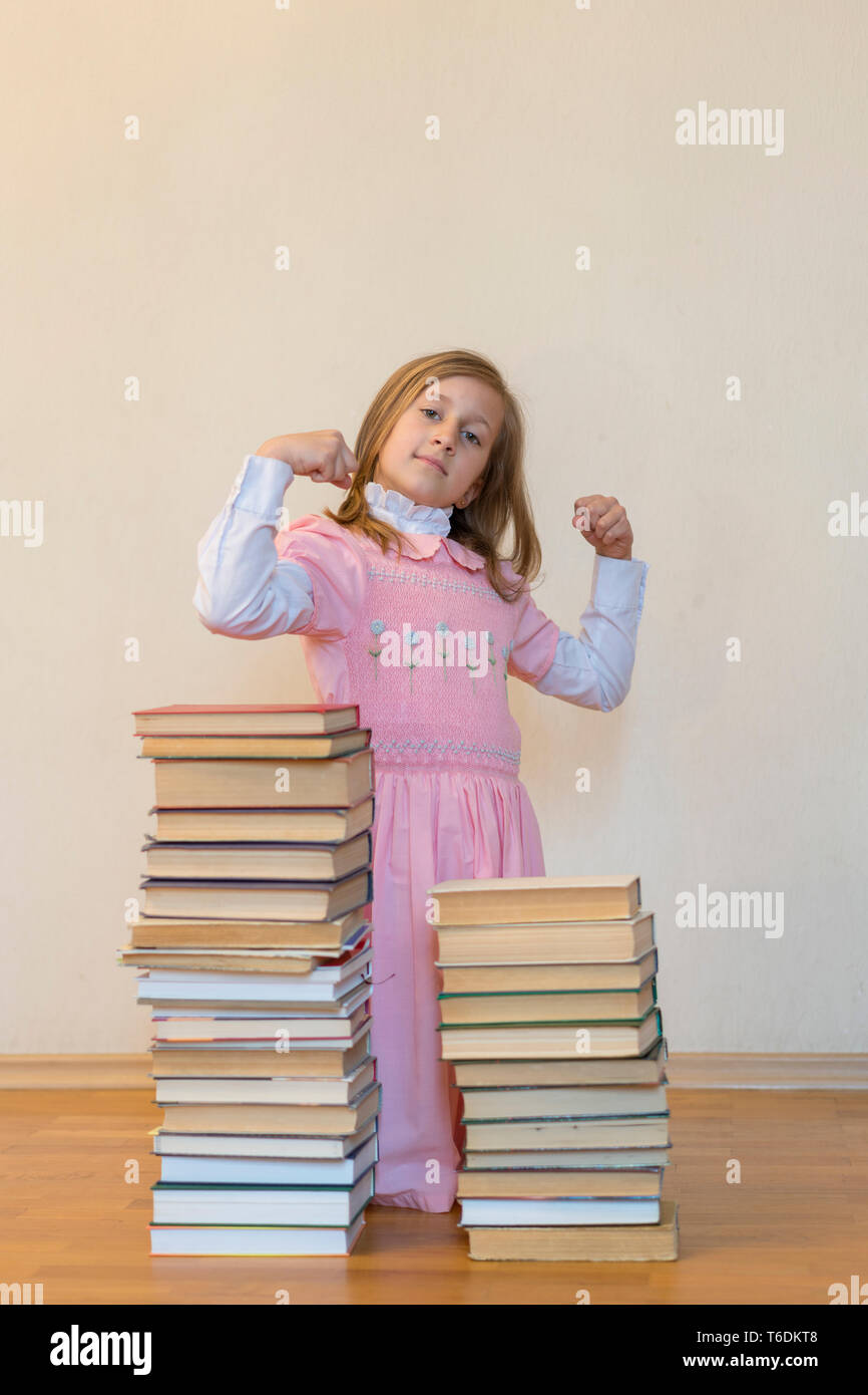 A little cute girl in a pink dress reading a book sitting on the floor ...