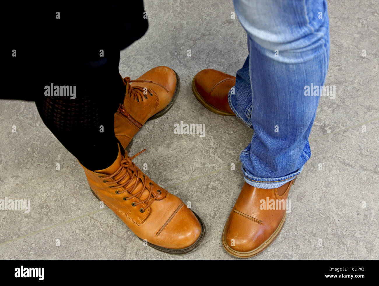 Two pair of feet with light brown leather boots on grey background ...