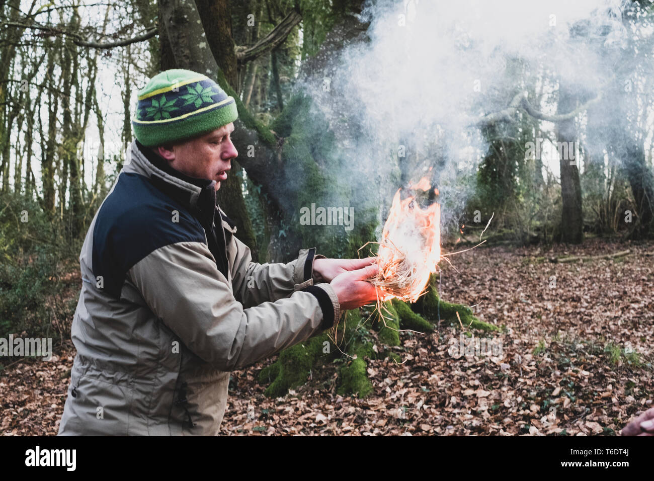 Man standing in a forest, holding lit-up bundle of straw, igniting fire ...