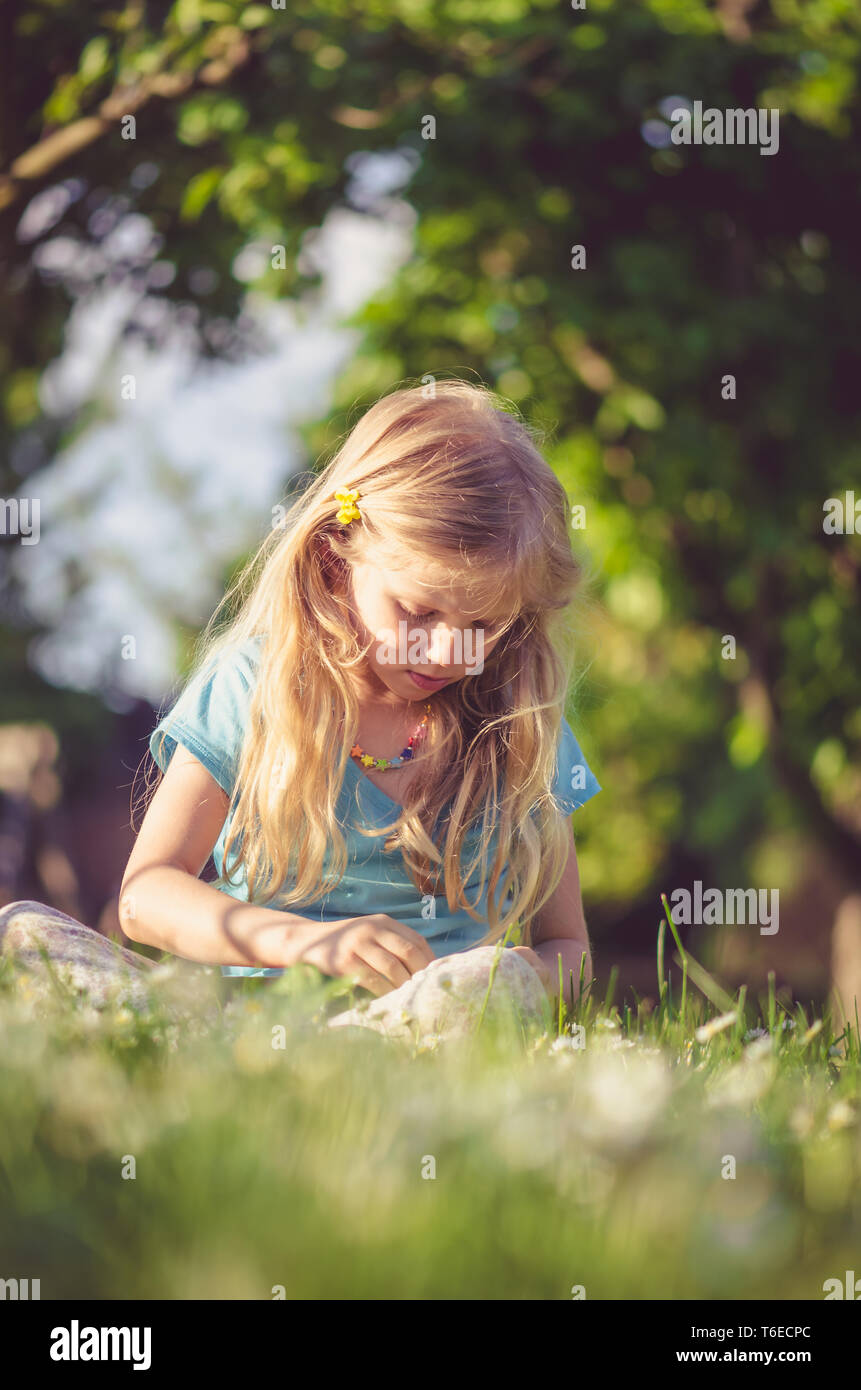 adorable blond girl sitting in spring meadow Stock Photo - Alamy